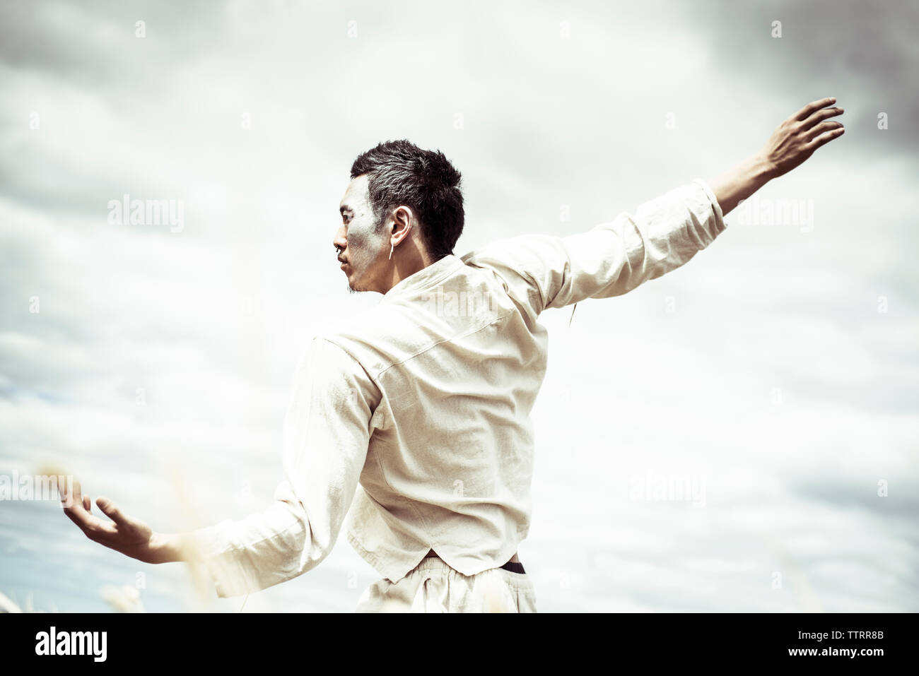 Rear view of man with arms outstretched dancing against cloudy sky at ...