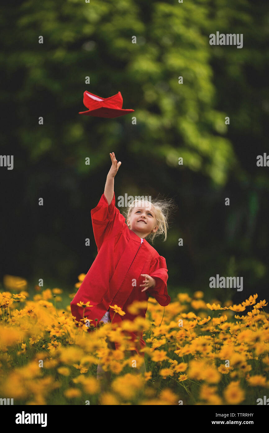 Girl wearing graduation gown throwing cap standing amidst yellow ...