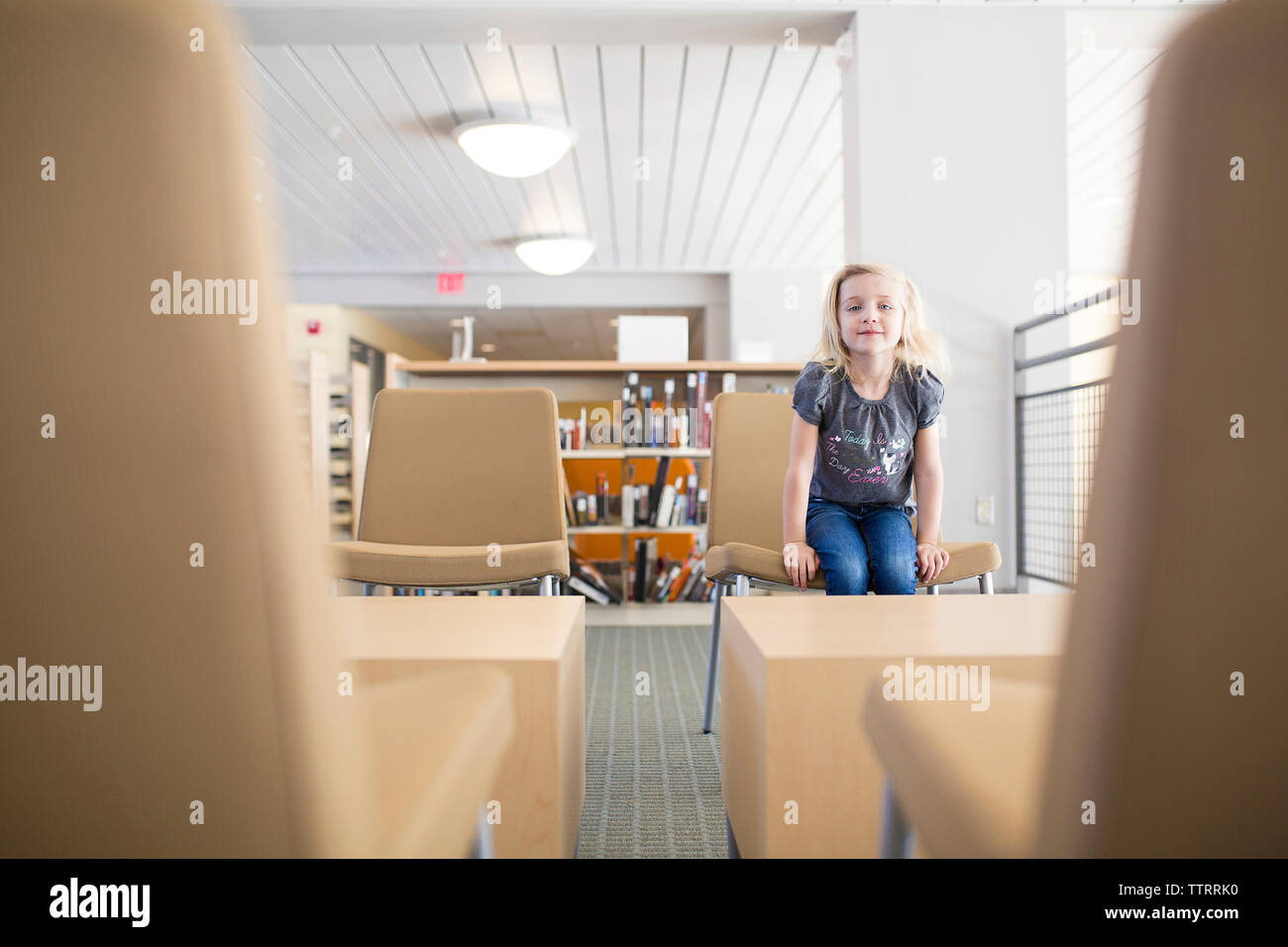 Portrait of smiling girl sitting on chair at library Stock Photo - Alamy