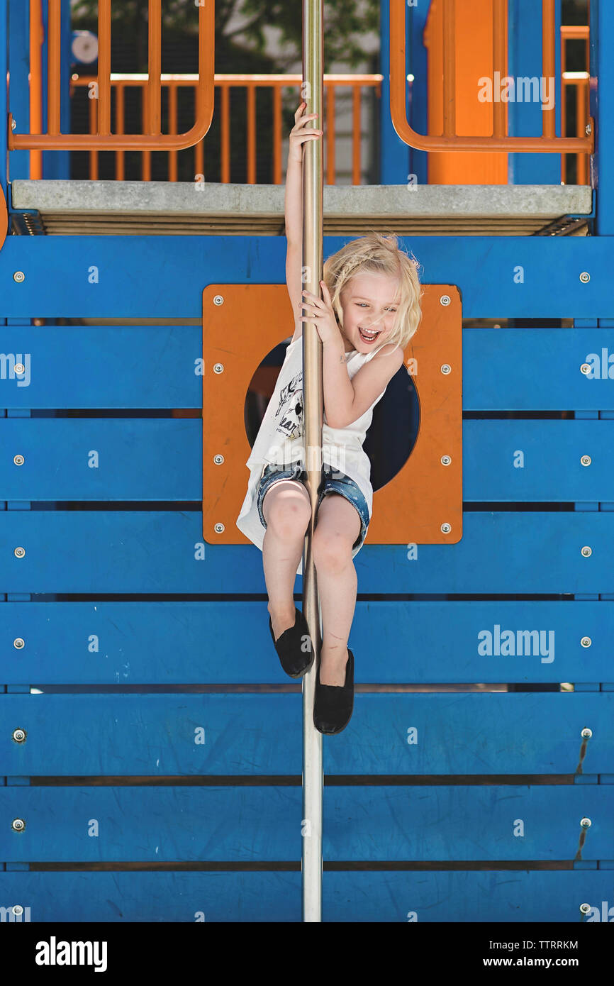 Cute girl playing on pole against wooden structure at playground Stock ...