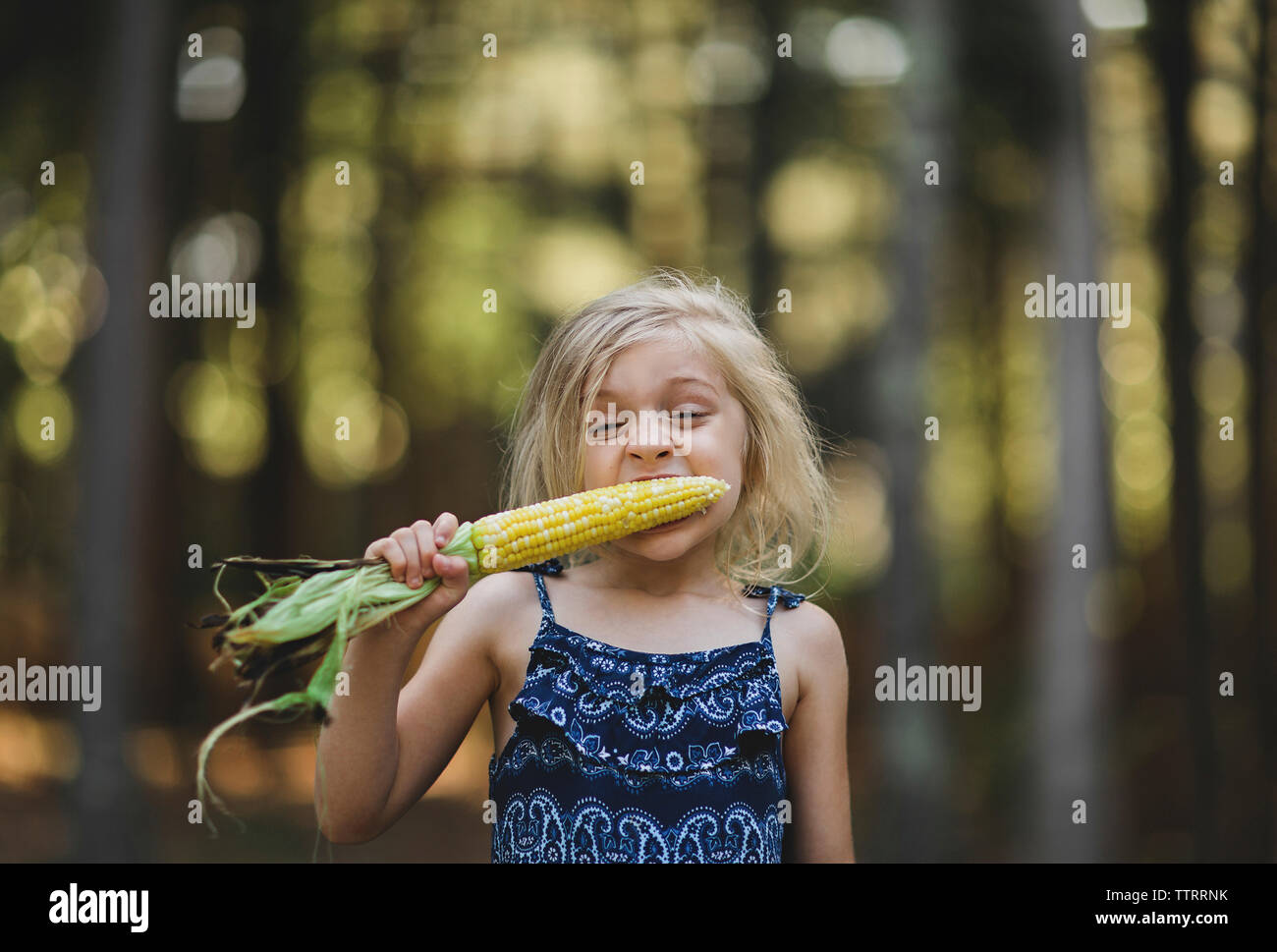 Girl eating corn while standing against trees in yard Stock Photo - Alamy