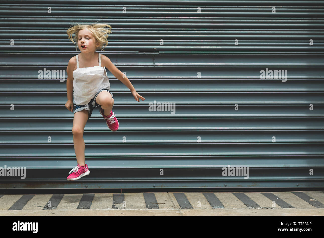 Girl jumping on sidewalk against shutter Stock Photo - Alamy