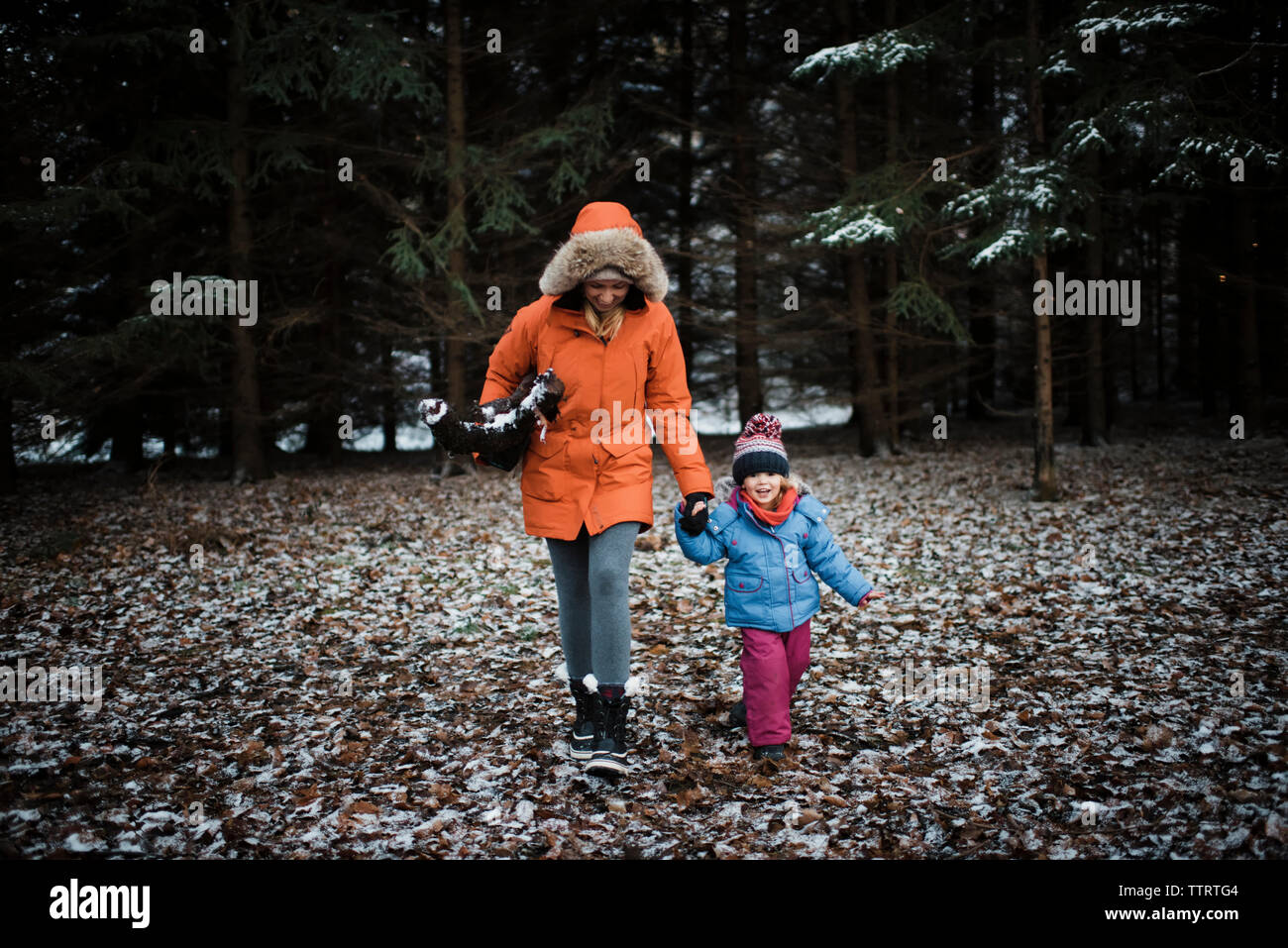 Mother and daughter in warm clothing walking at forest during winter ...