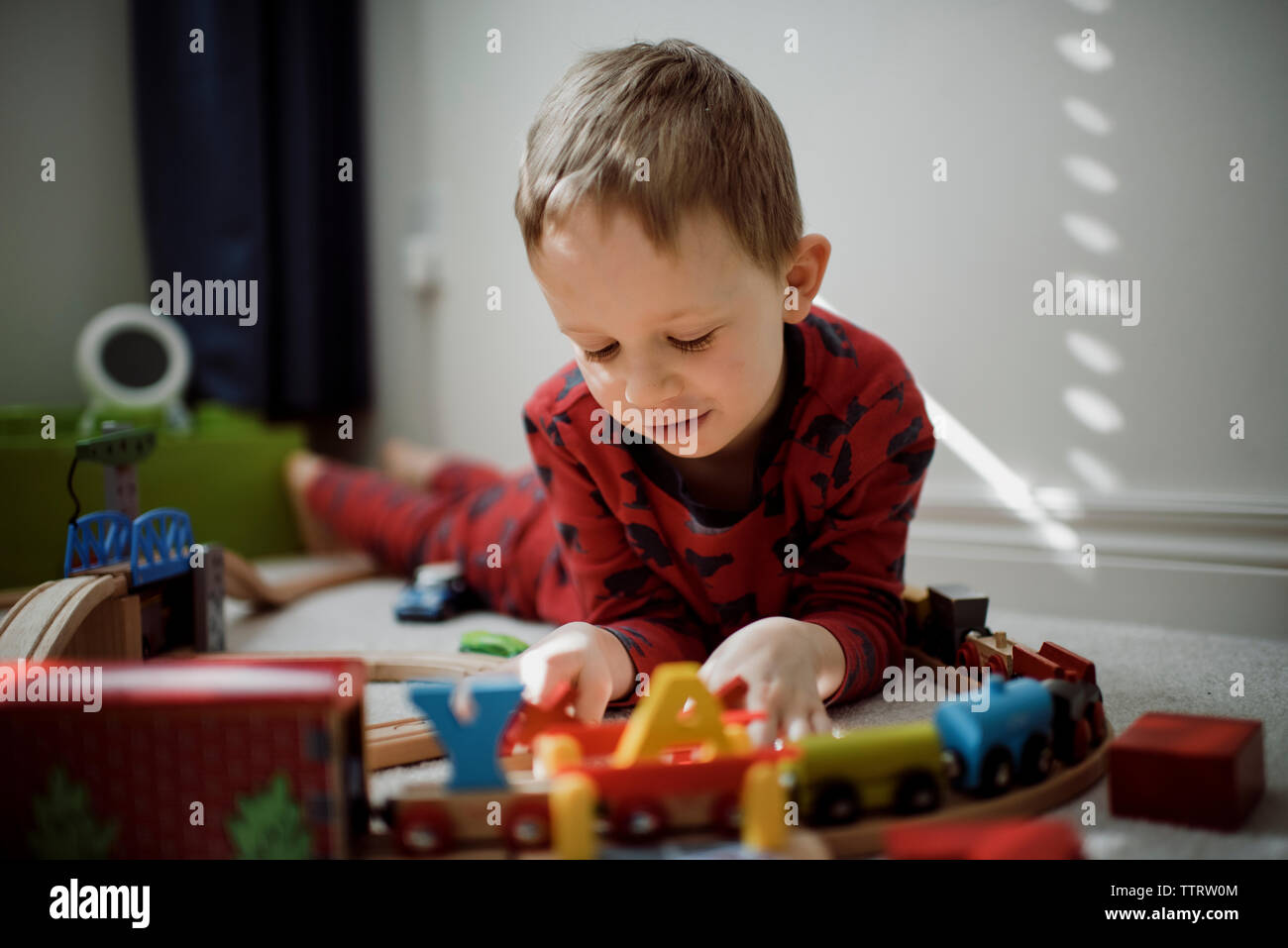 Cute boy playing with model train set while lying on carpet at home ...