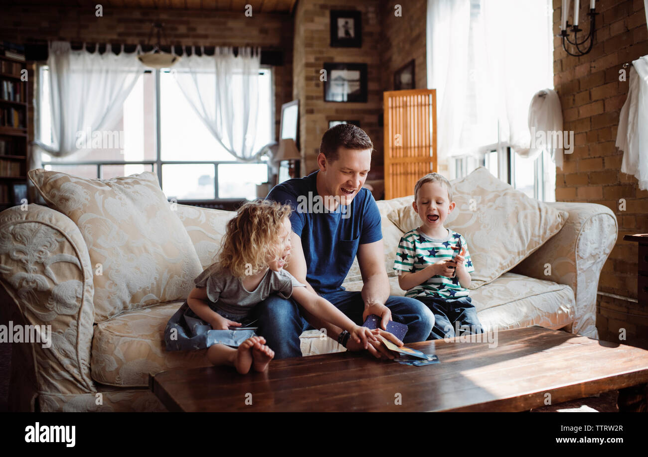 Happy father playing with children while sitting on sofa in living room ...