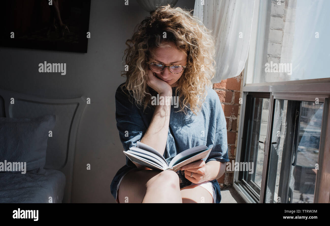 Woman reading book while sitting on window sill at home Stock Photo - Alamy
