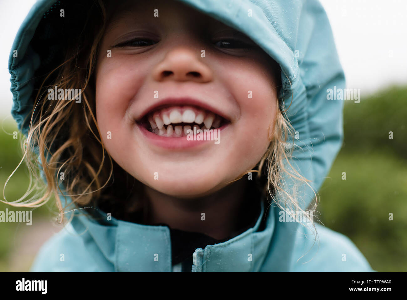 Close-up portrait of cute happy girl in blue raincoat standing against ...