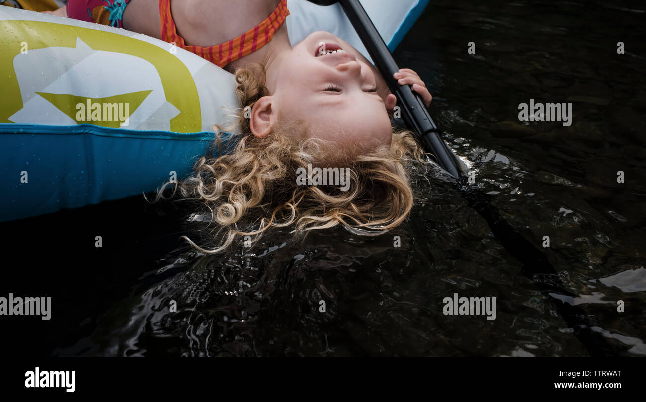 High angle view of happy cute girl lying in inflatable raft on lake ...