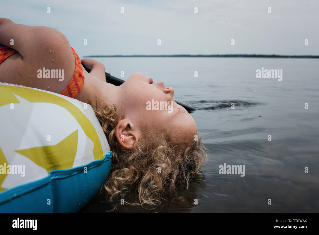 Side view of cute girl with eyes closed lying in inflatable raft on ...