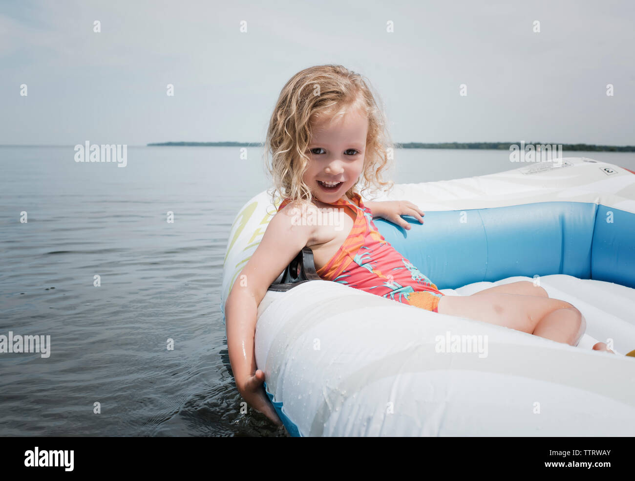 Portrait of cute girl sitting in inflatable raft on lake against sky ...