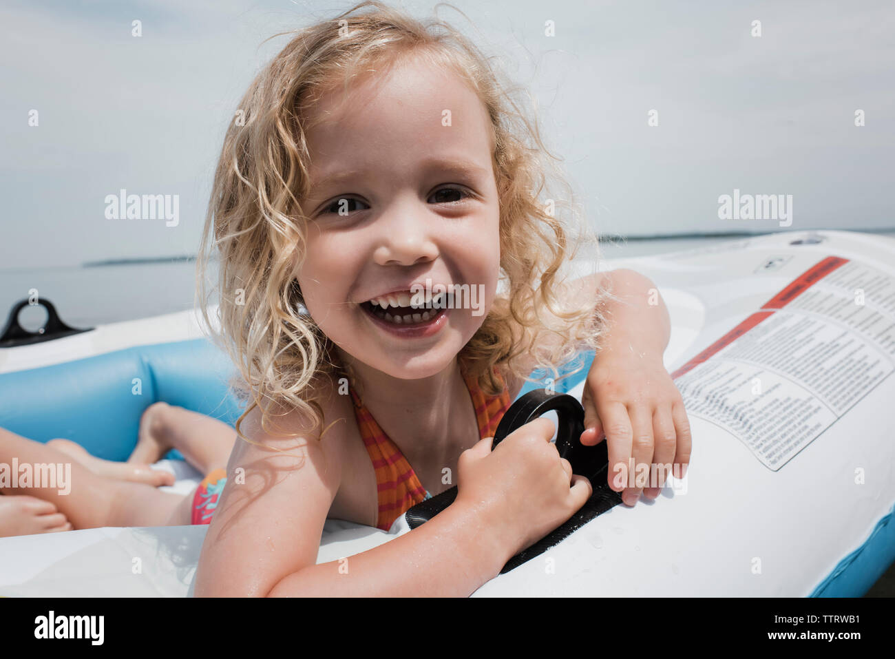 Portrait of cute happy girl lying in inflatable raft on lake against ...