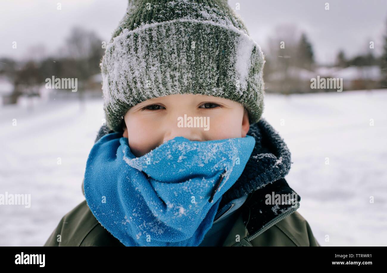 young boy aged 6 standing in the snow with snow on his face and hat ...