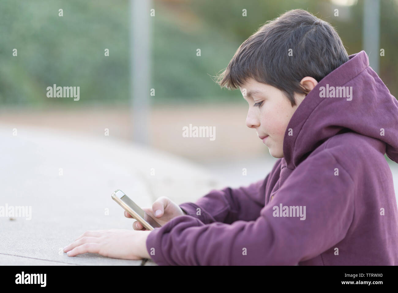 Side view of boy using mobile phone while sitting outdoors Stock Photo ...