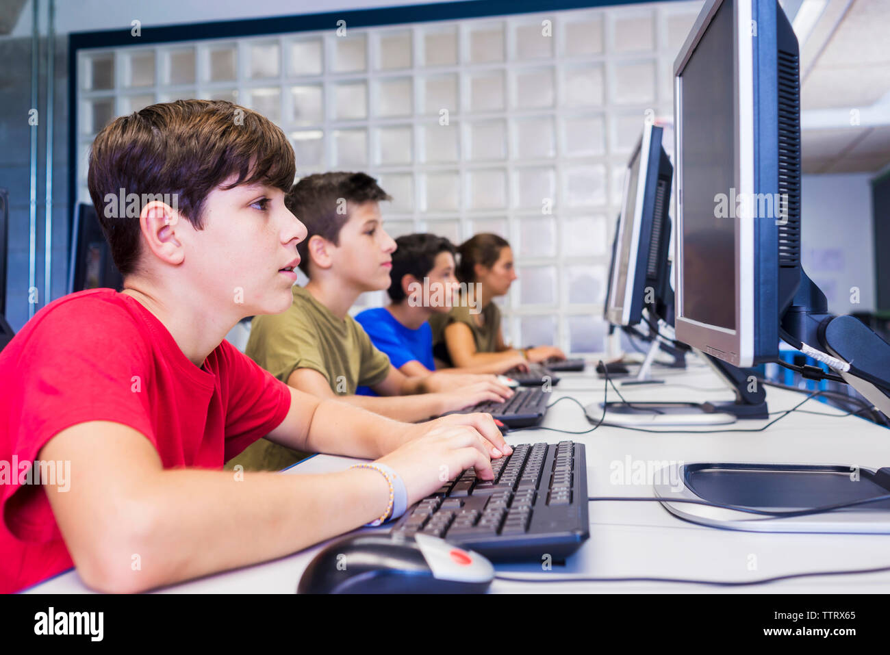 Side view of teacher with students using computers in classroom Stock ...
