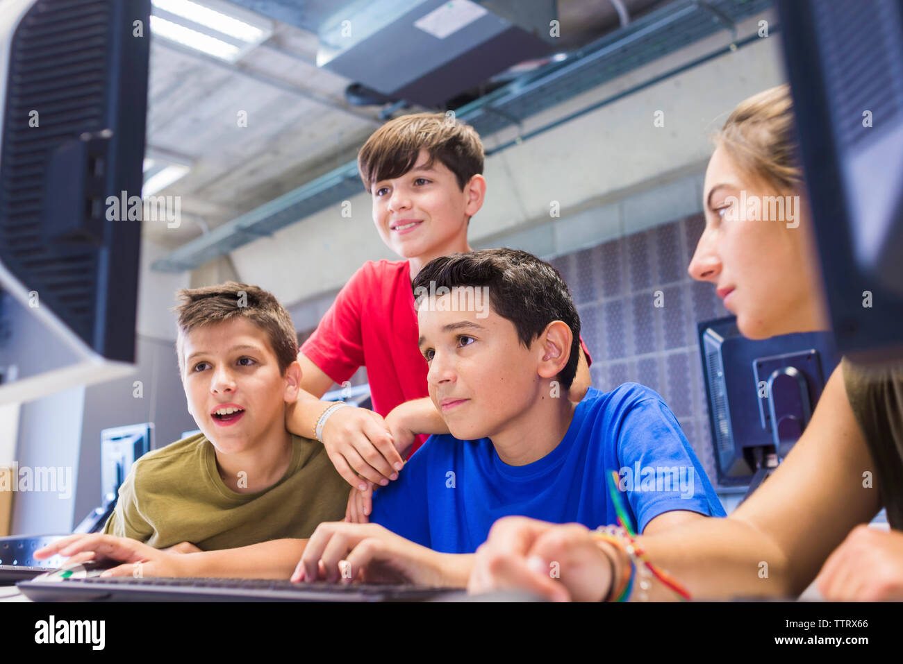 Low angle view of teacher teaching students over desktop computer in ...