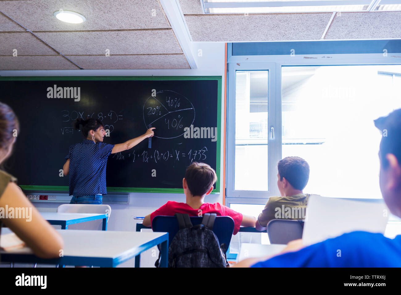 Rear view of female teacher explaining mathematics to students in ...