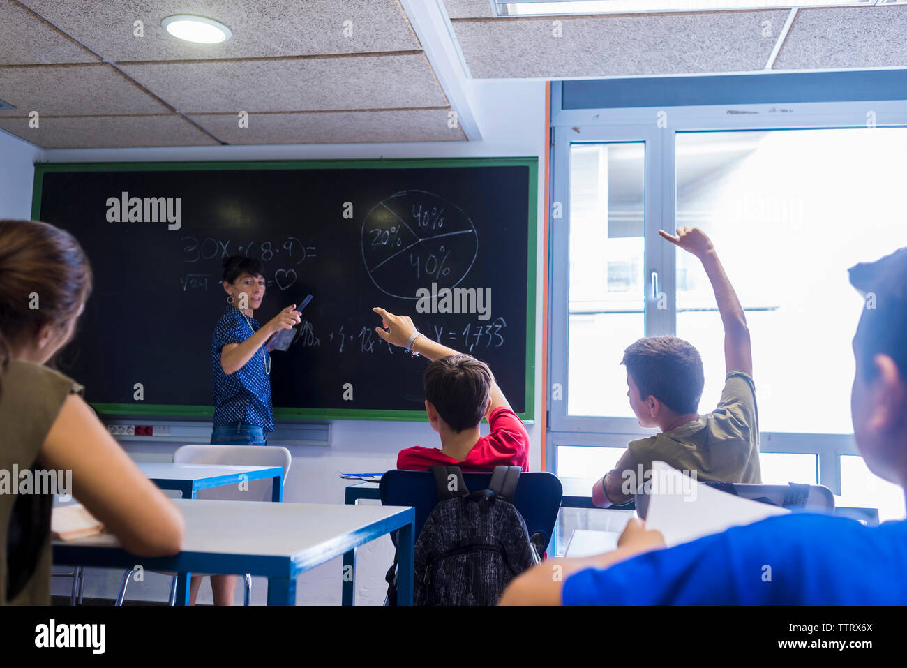 Side view of female teacher interacting with students in classroom ...