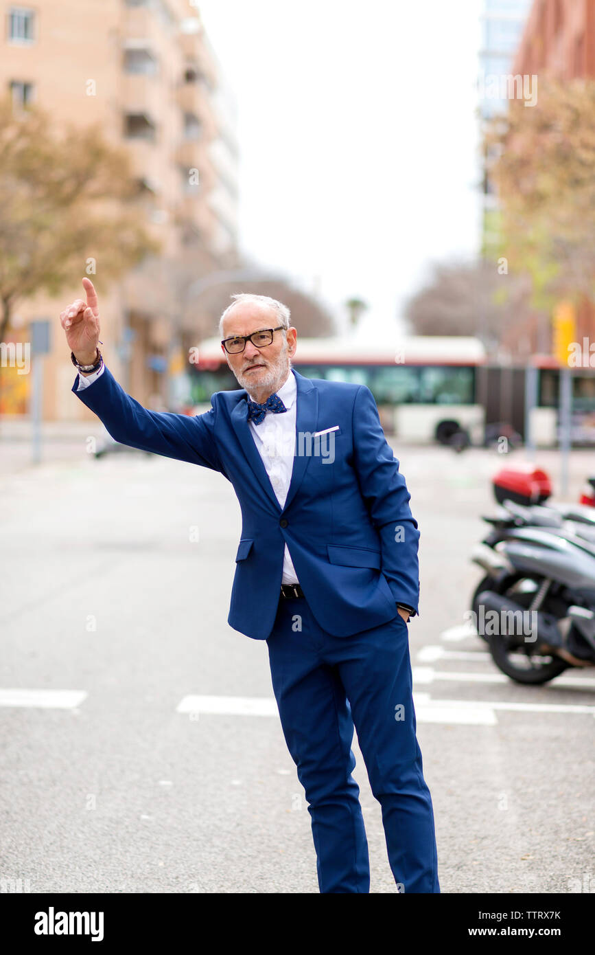 Confident senior man in suit hailing while standing on city street ...