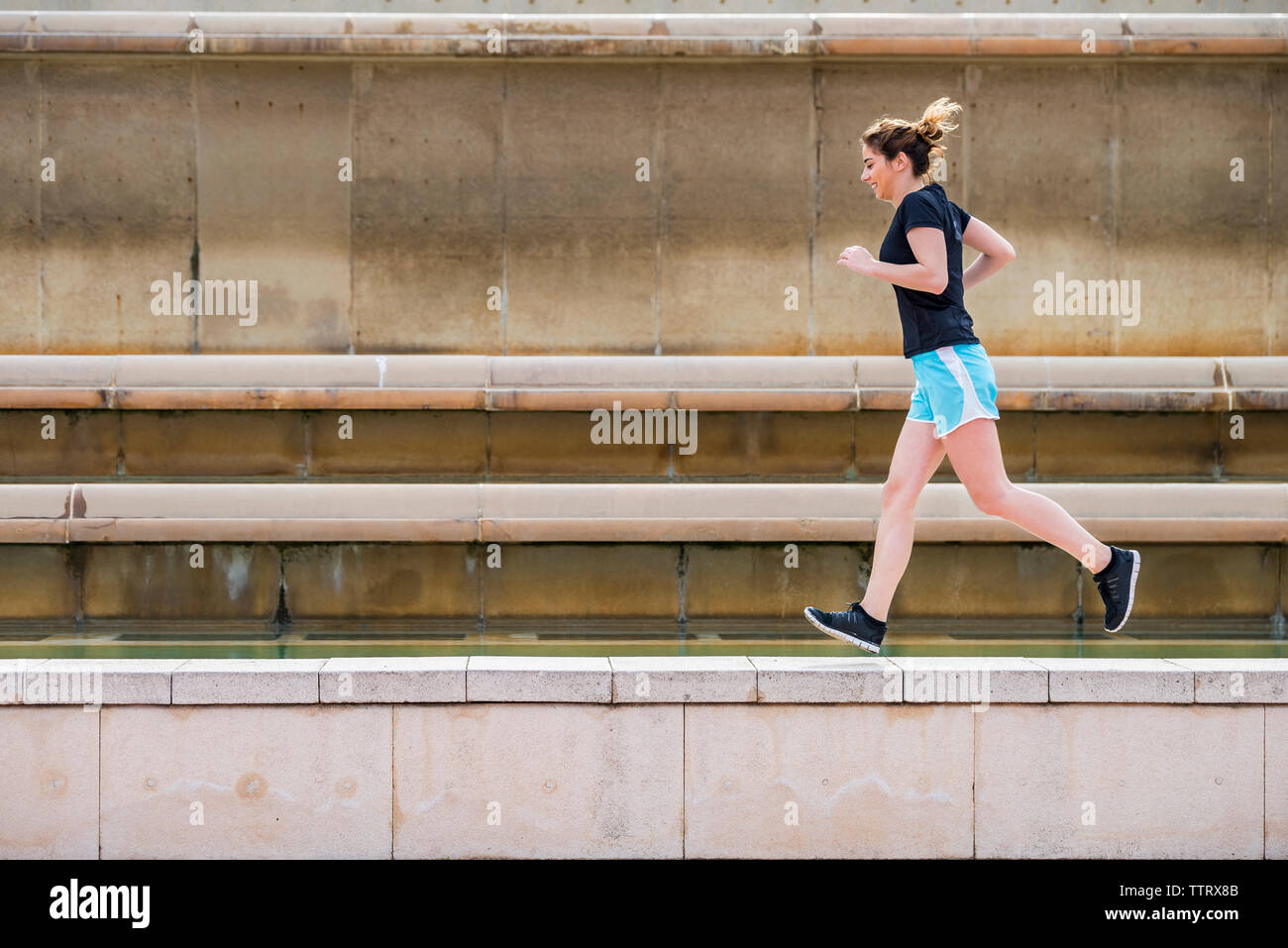 Side view of woman running on retaining wall against wall at park Stock ...