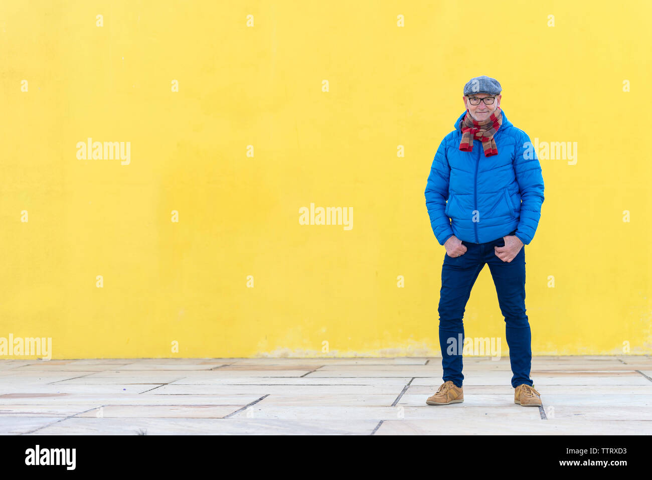 Confident senior man in casual clothes standing against yellow wall ...