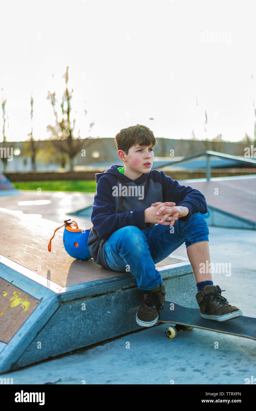 Front view of young skater sitting at skateramp while looking away ...