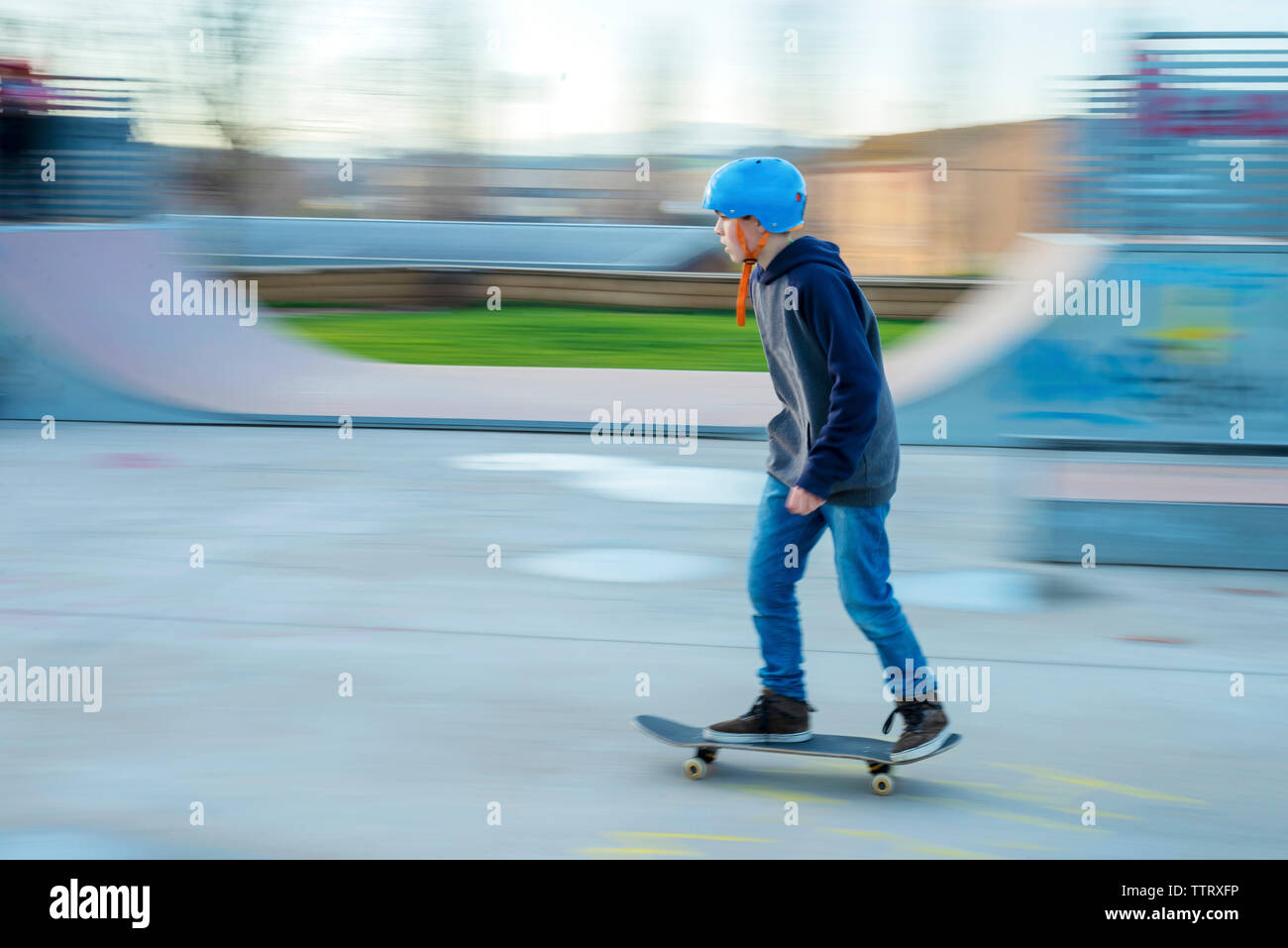 Side view of young skater wearing blue helmet in motion at skatepark ...