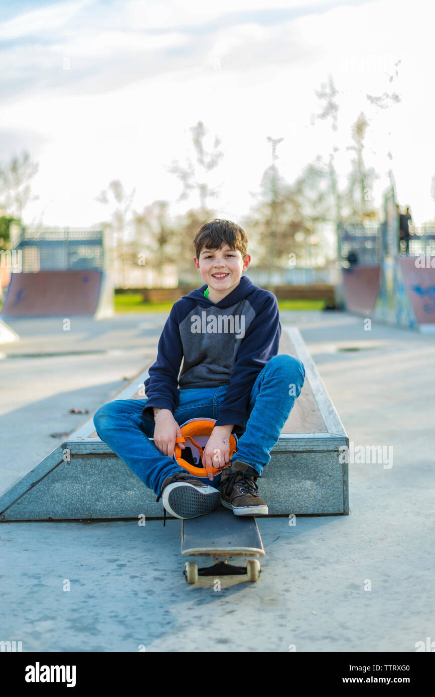 Front view of young smiling boy sitting at skatepark, looking camera ...