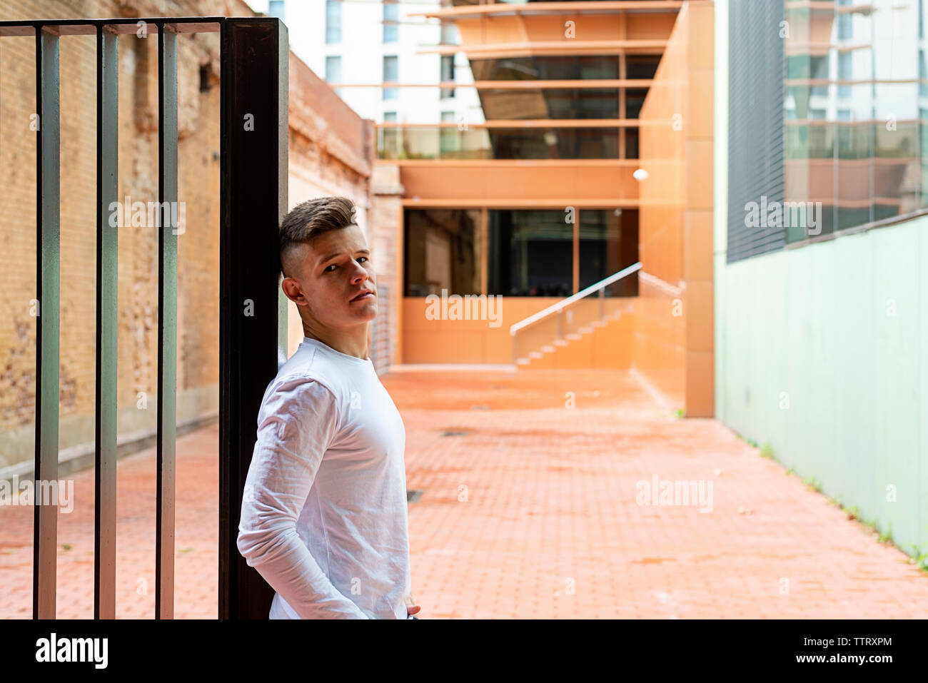 Side view young man leaning on a fence while looking camera Stock Photo ...