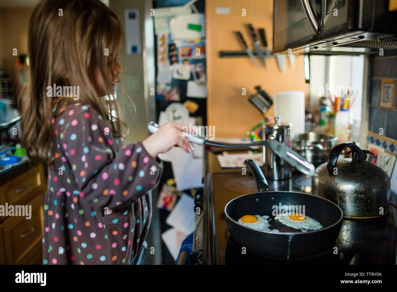 Side view of girl cooking eggs in frying pan at kitchen Stock Photo - Alamy