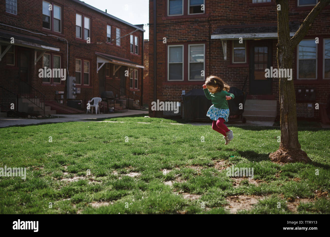 Full length of playful girl jumping on grass against house at front ...