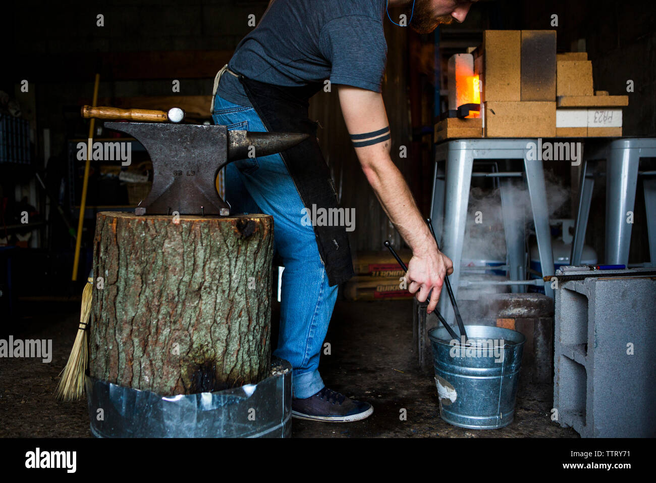 Blacksmith putting tongs in bucket of water at workshop Stock Photo - Alamy