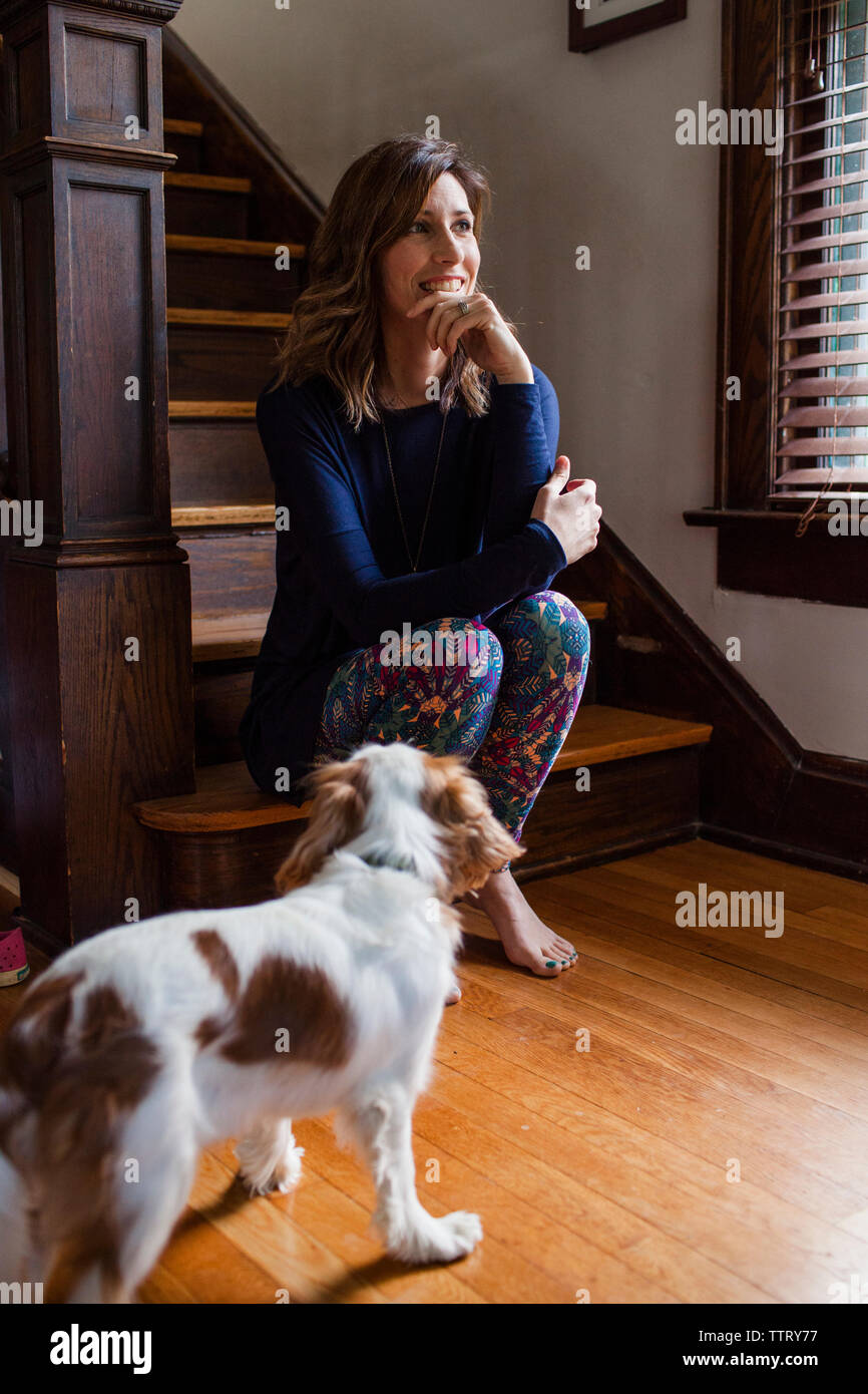 Dog standing by smiling woman sitting on steps at home Stock Photo - Alamy