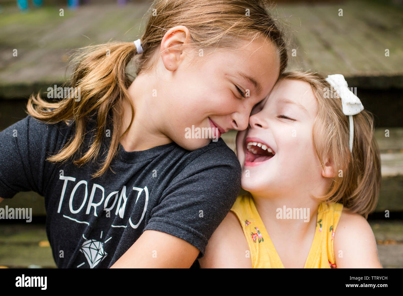 Happy cute sisters looking at each other while sitting on steps in yard ...