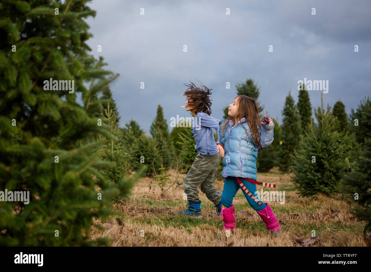 Side view of happy siblings dancing on grassy field against cloudy sky ...