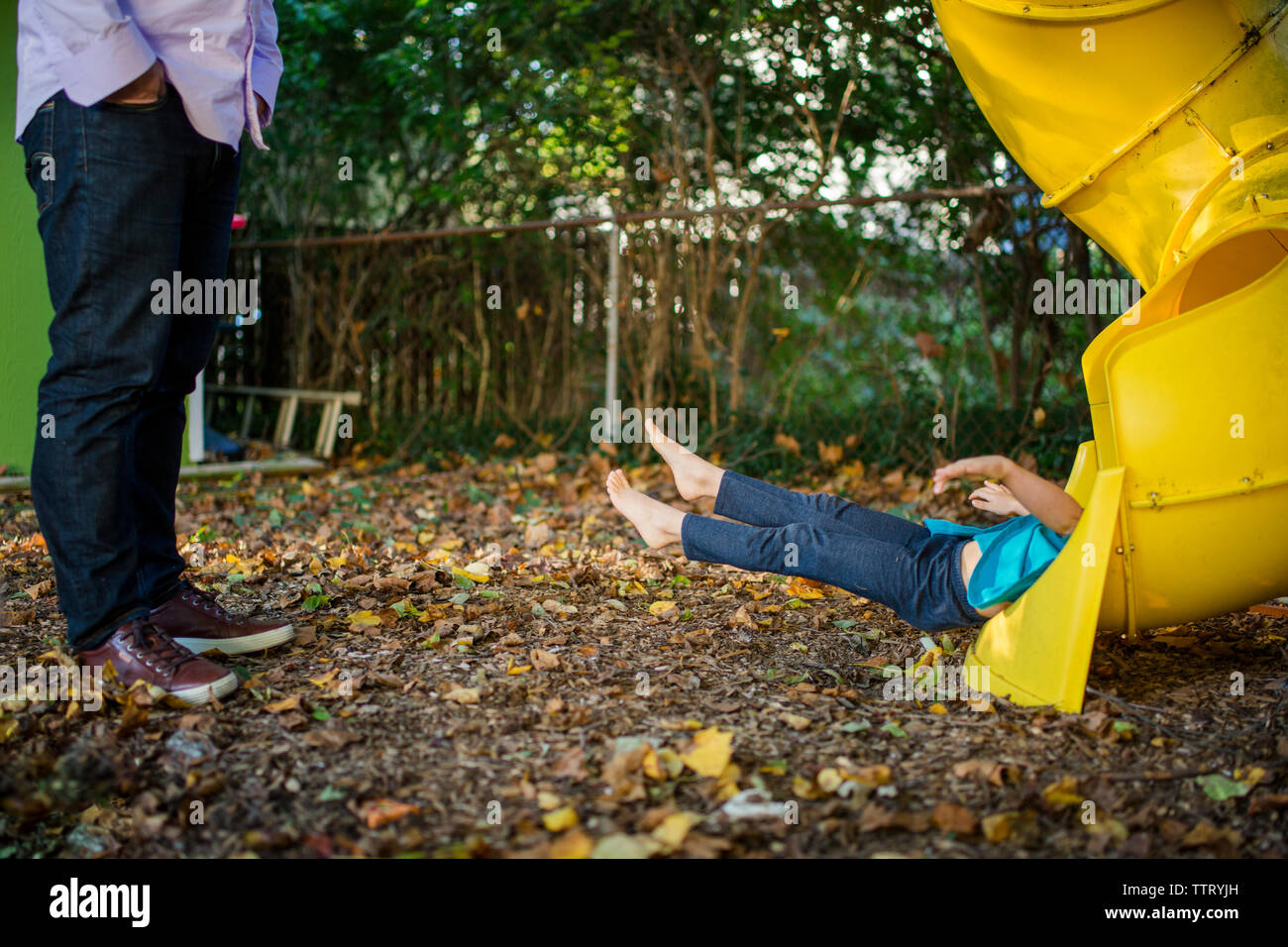 the bottom half of a child emerges from a slide as her father watches ...