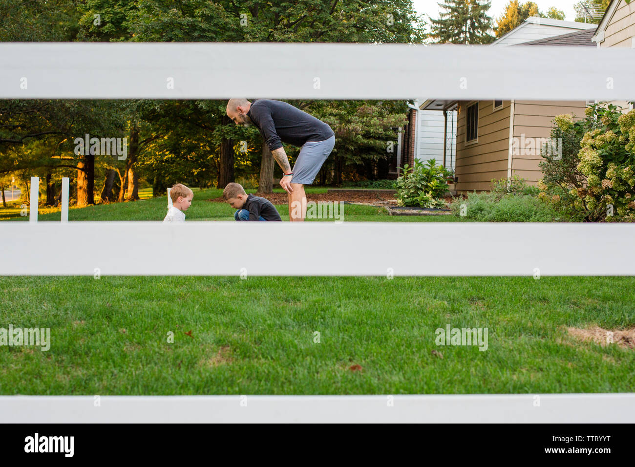 view through a fence of a father playing with children in yard Stock ...
