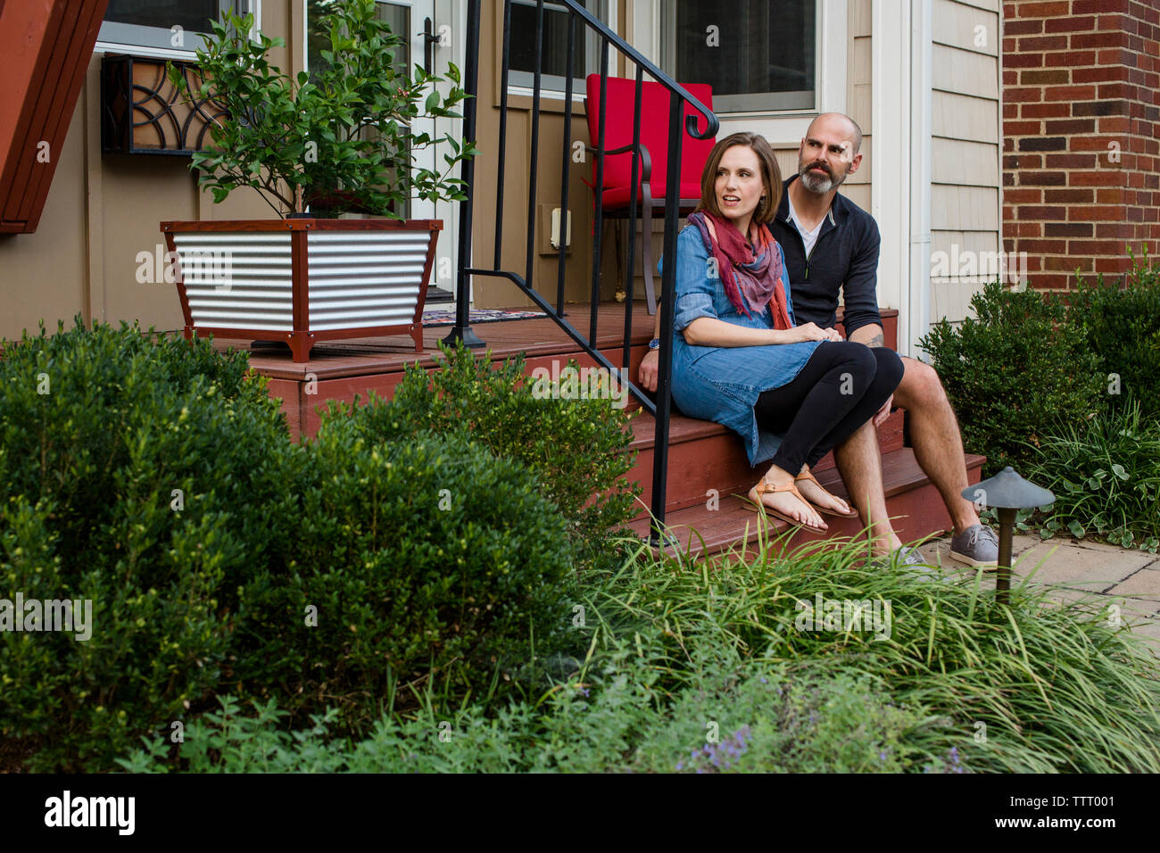 A couple sit on their front stoop together looking off to the side ...