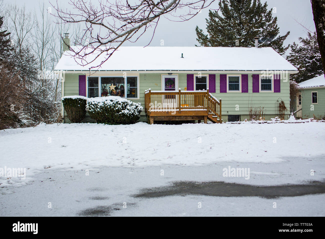 Front view of a cheerful house in a snowy yard with children in window ...