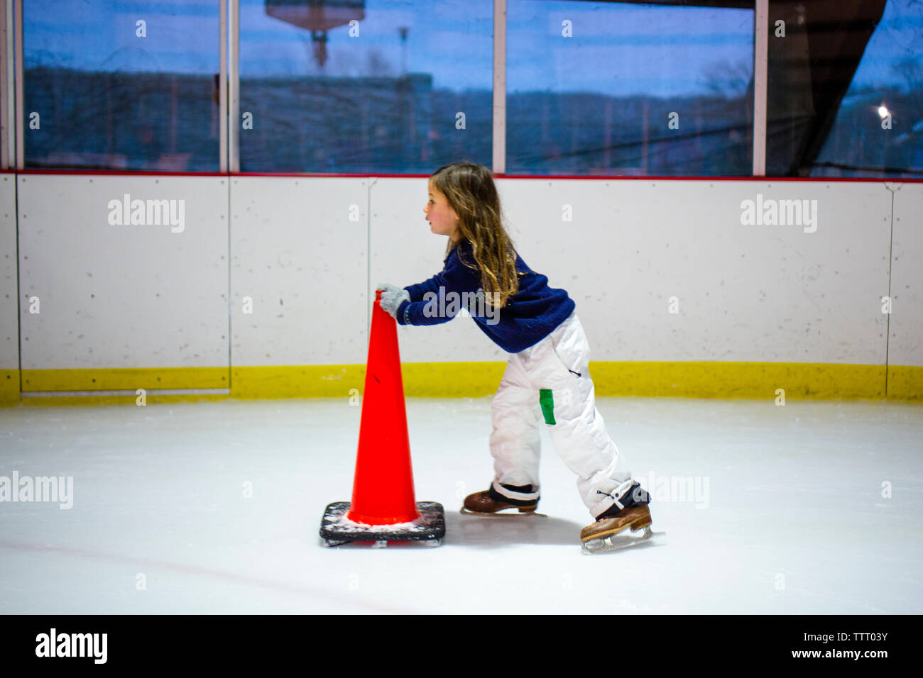 A little girl in snow pants and ice skates skates alone in an ice rink ...