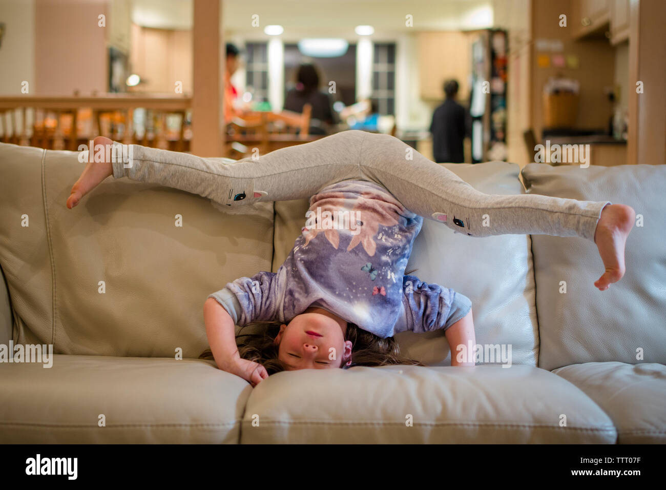 Portrait of cute little girl tumbling on the couch with family in back ...