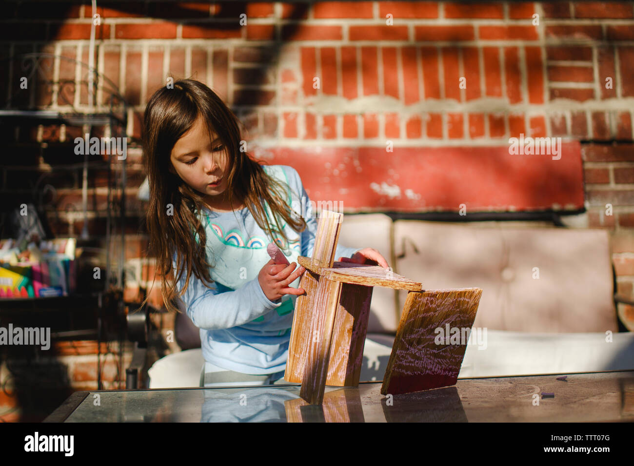 A focused child concentrates on building with wood against brick wall ...