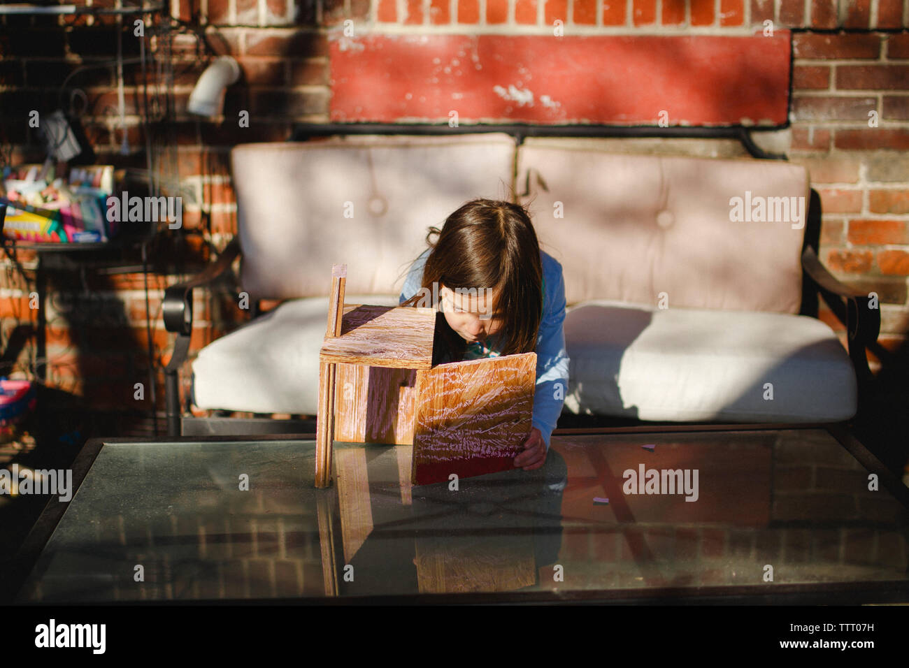 A small child on a patio leans over to inspect her wooden building ...