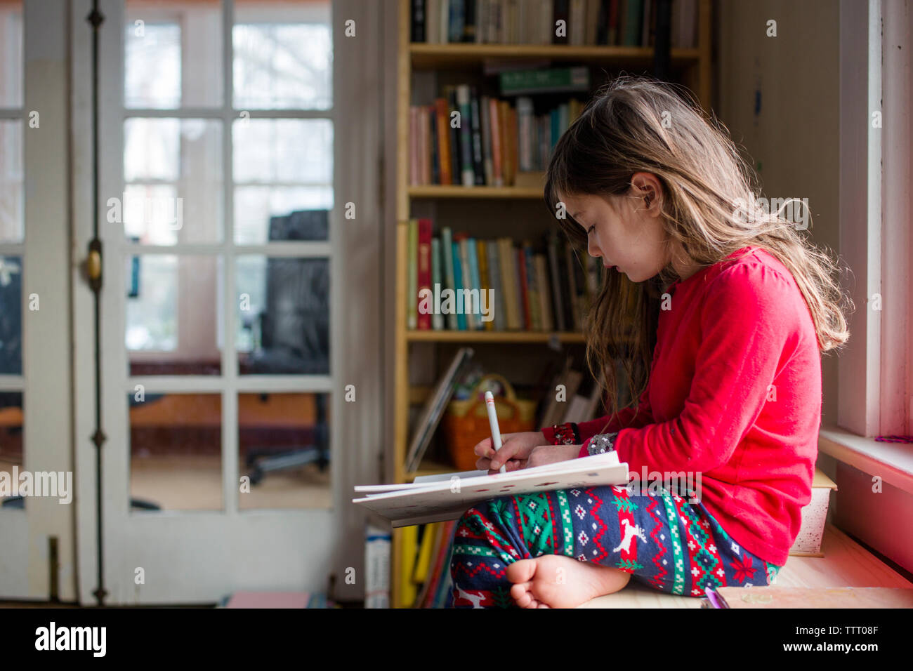 Side view of a focused little girl drawing with marker in a notebook ...