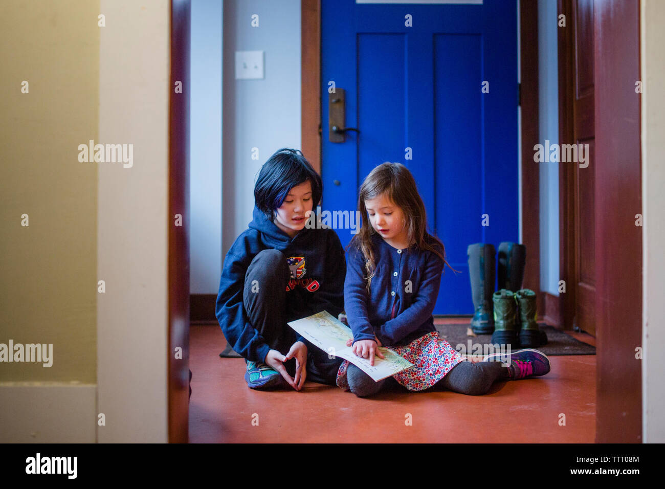 two children sit in the foyer of their home reading a book together ...