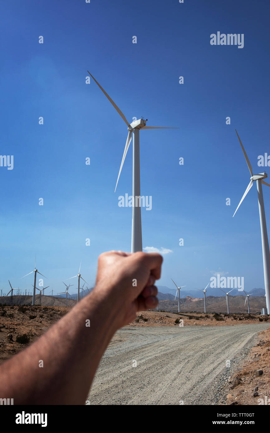 Optical illusion of man's hand holding wind turbine against blue sky ...