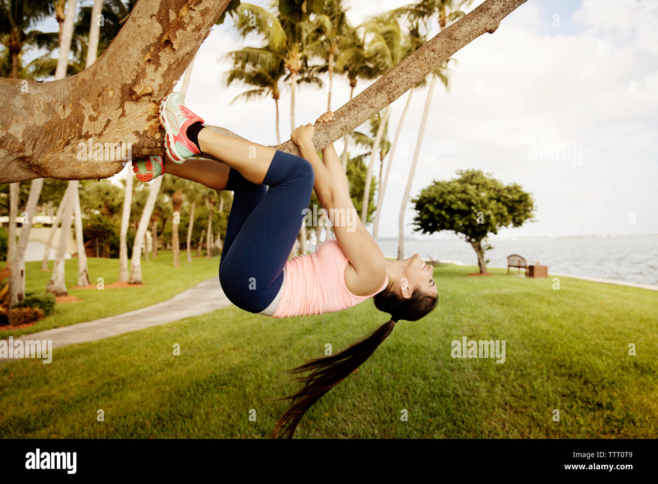 Side view of woman hanging on tree branch at grassy field Stock Photo ...