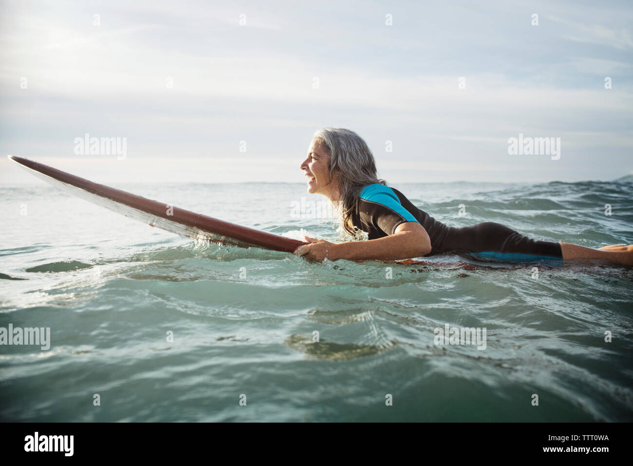 Side view of happy female surfer lying on surfboard in sea Stock Photo ...