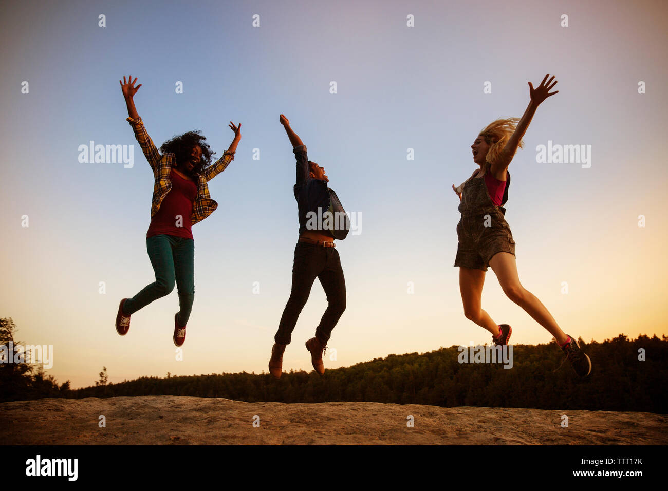 Friends jumping on rock against clear sky during dusk Stock Photo - Alamy