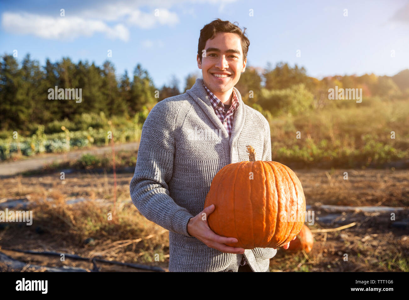 Portrait of man carrying pumpkin while standing in farm against sky ...