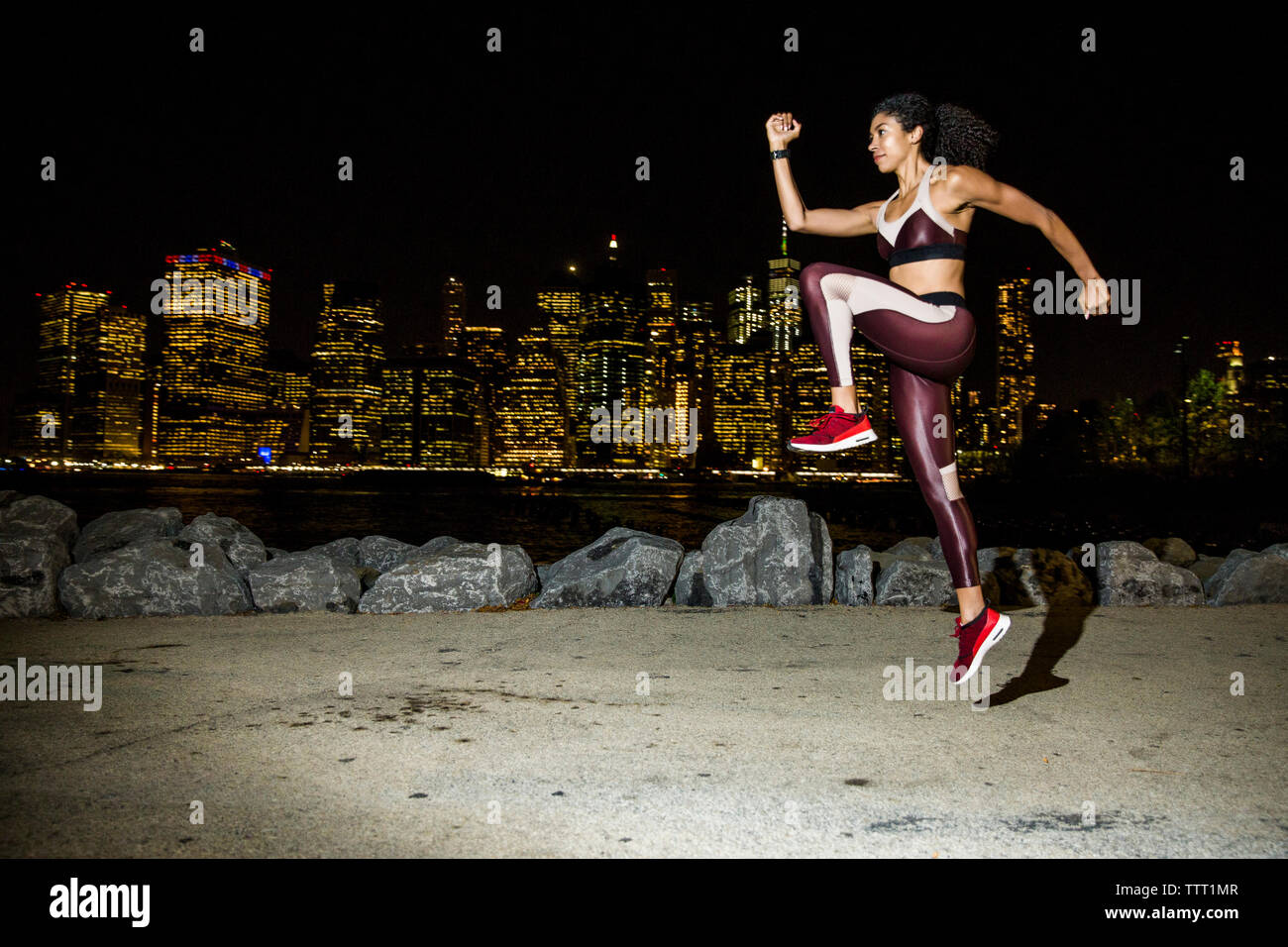 Female athlete jumping against illuminated buildings at night Stock ...